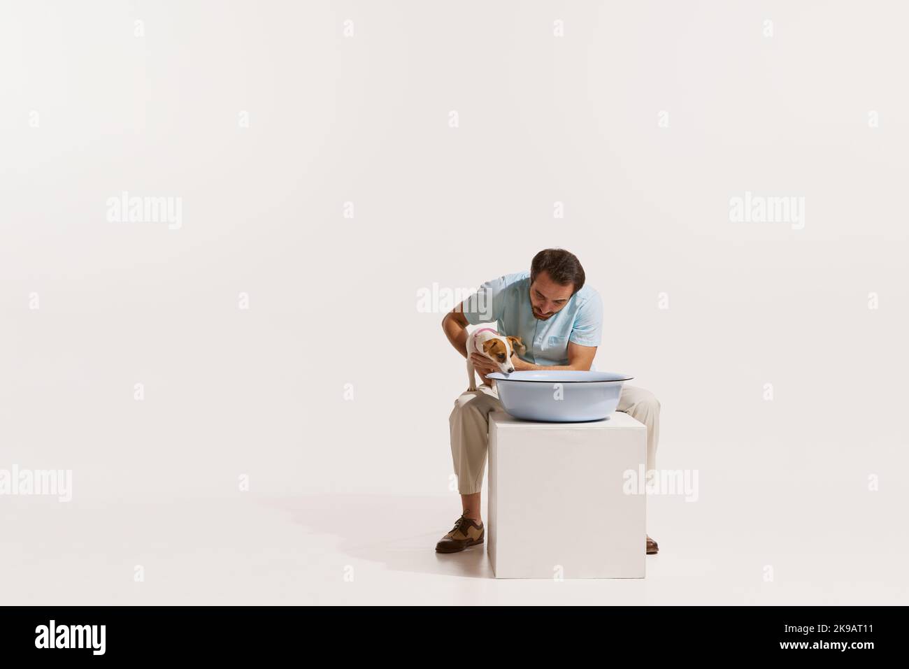 Portrait of young man sitting with dog and doing washing up isolated ...