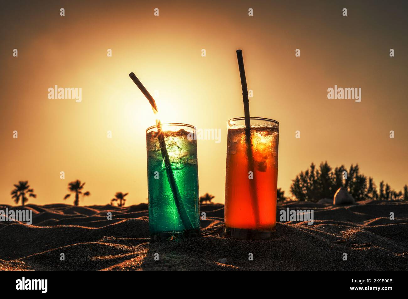 Colorful alcoholic drinks with a straw in the sand with palm trees at ...
