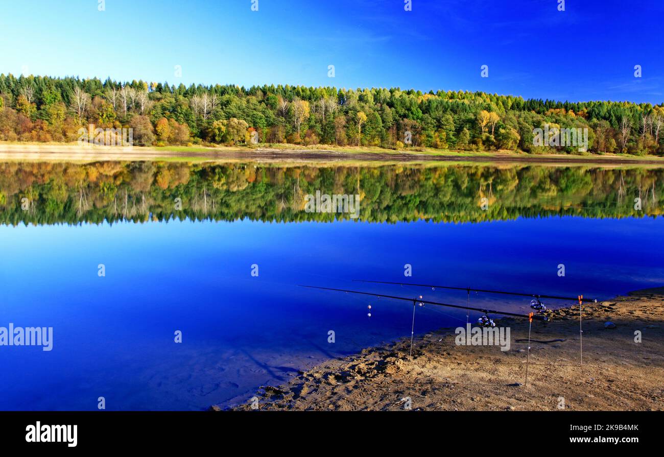 Fishing rod and reflection of colorful autumn trees on lake Stock Photo ...