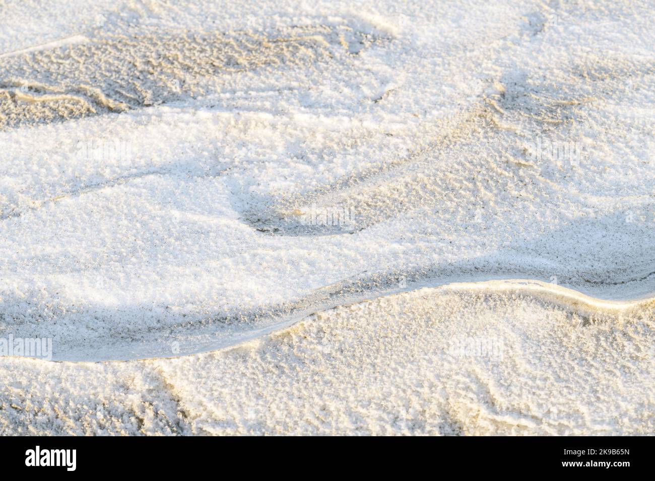 Pattern of snow covered ripples in the sand on the beach, lit by the ...