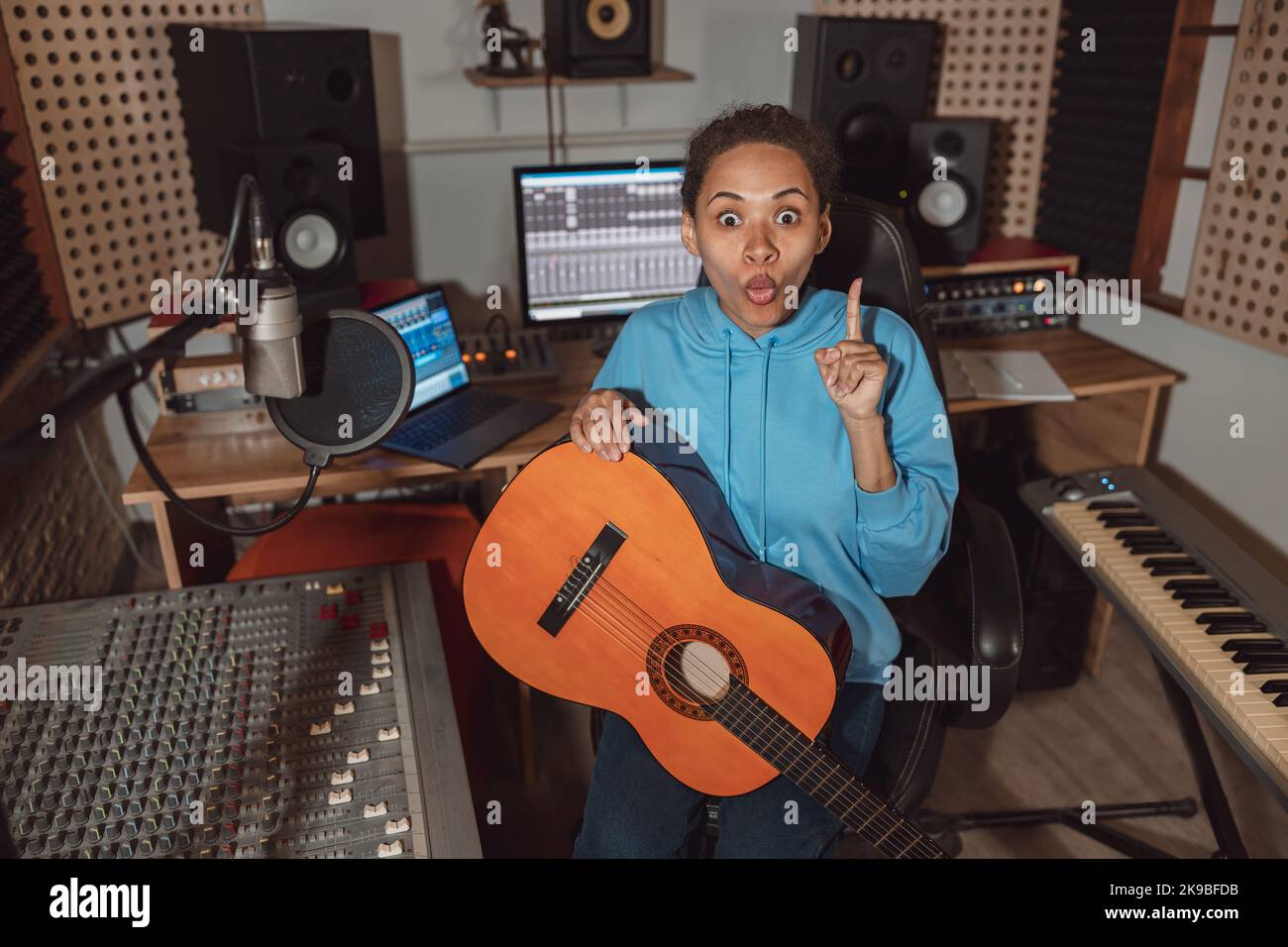 Astonished African musician with guitar points finger up while sitting ...