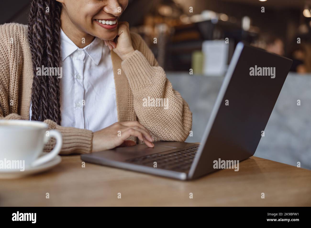 Cropped view to a cute ethnic woman smiling toothy smile while working on laptop during coffee ...