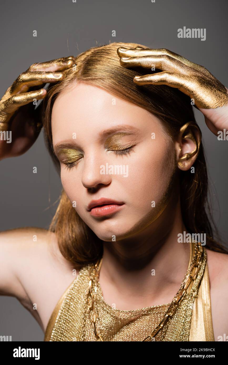 Young model with makeup and hands in golden paint touching hair ...