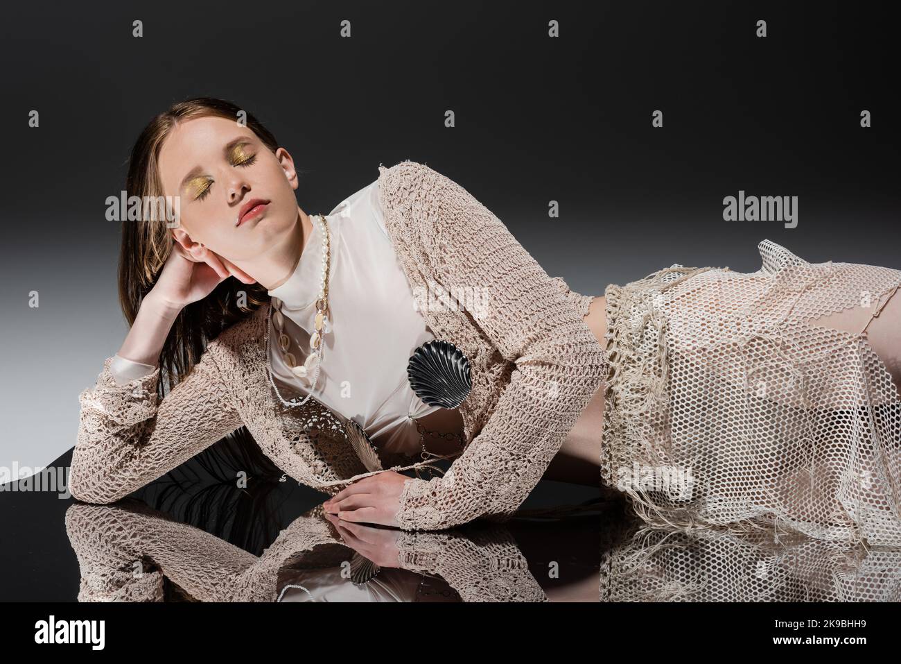 mermaid in knitted cardigan and fishnet skirt lying on mirror on grey ...