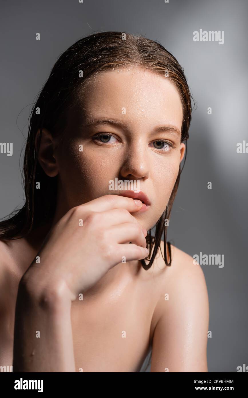 Portrait of woman with wet hair and skin touching lips on grey ...