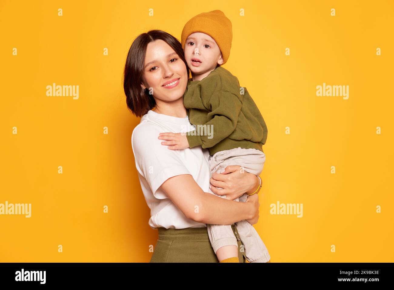 Happy young mother with her cute little son posing isolated on bright yellow background. Family ...