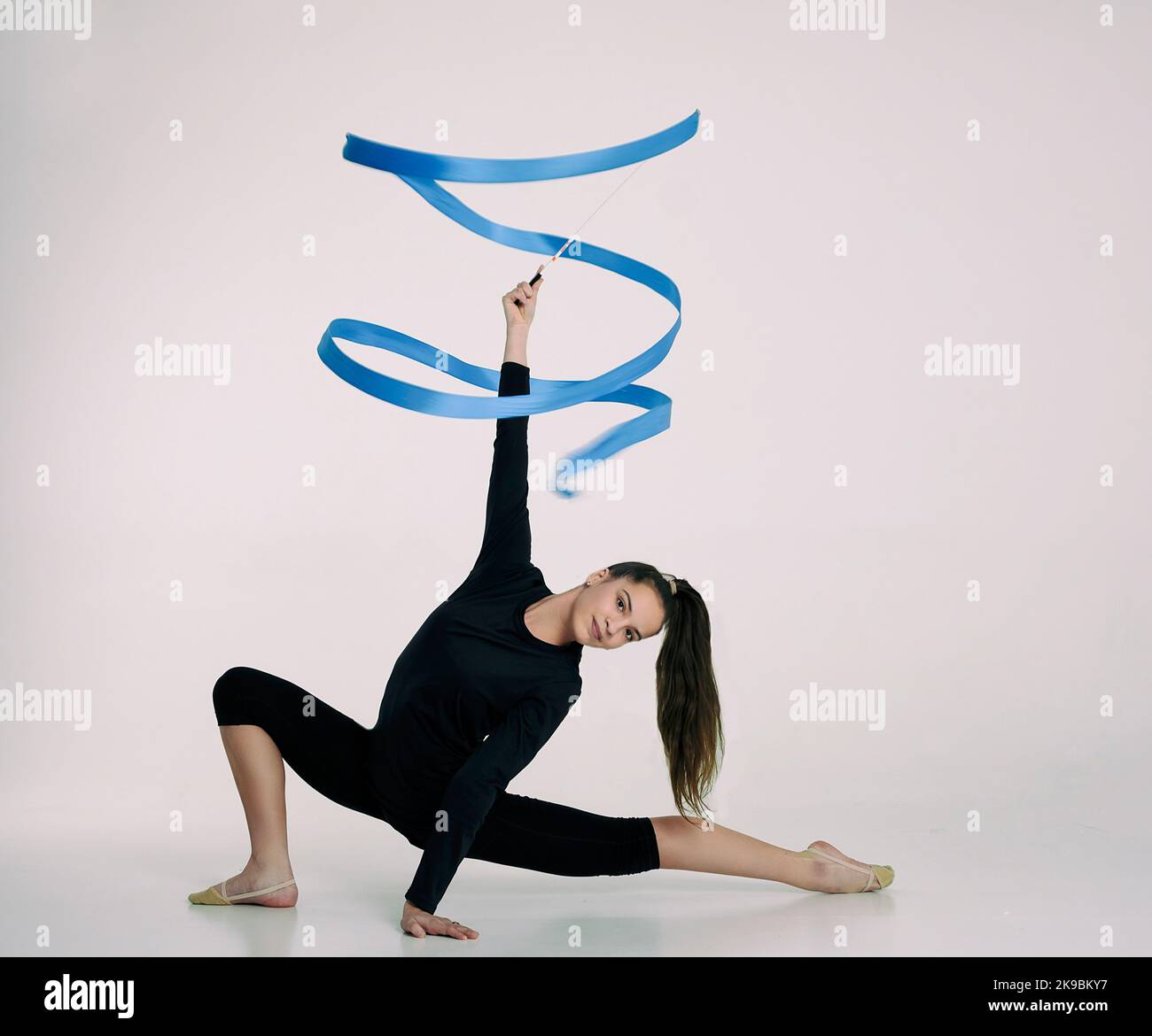a girl from rhythmic gymnastics in a bodysuit rotates a ribbon sitting ...