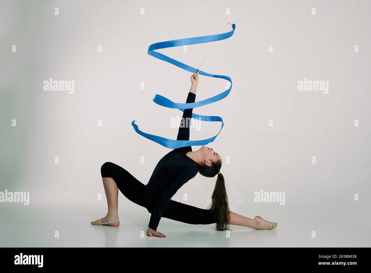 a girl from rhythmic gymnastics in a bodysuit rotates a ribbon sitting ...