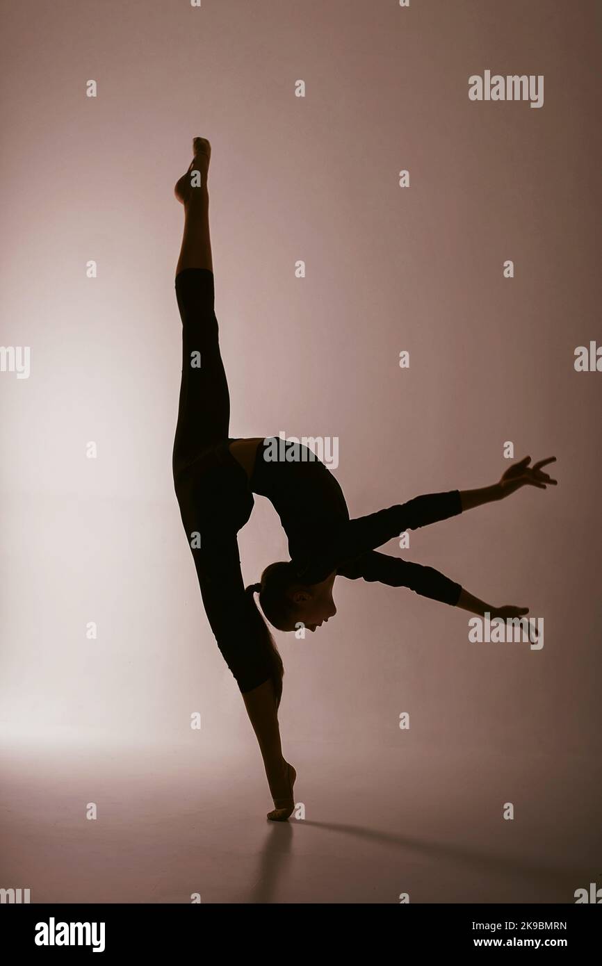 the silhouette of a rhythmic gymnastics girl in a bodysuit shows an ...