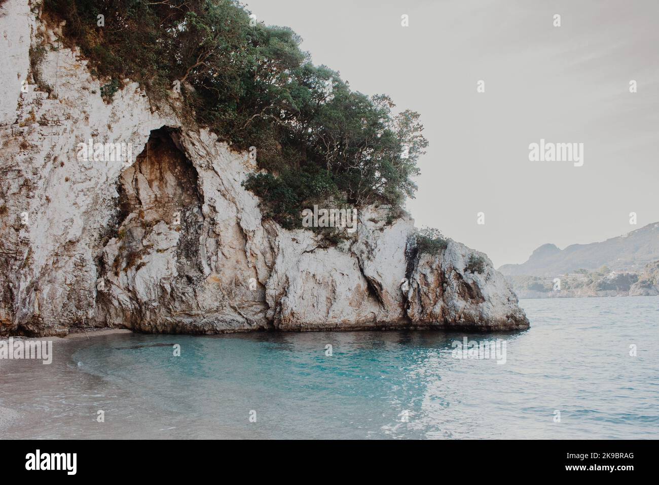Corfu, Greece. A huge rock on the beach with blue water on which green ...