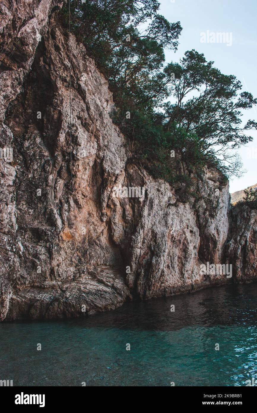 Corfu, Greece. A huge rock on the beach with blue water on which green ...