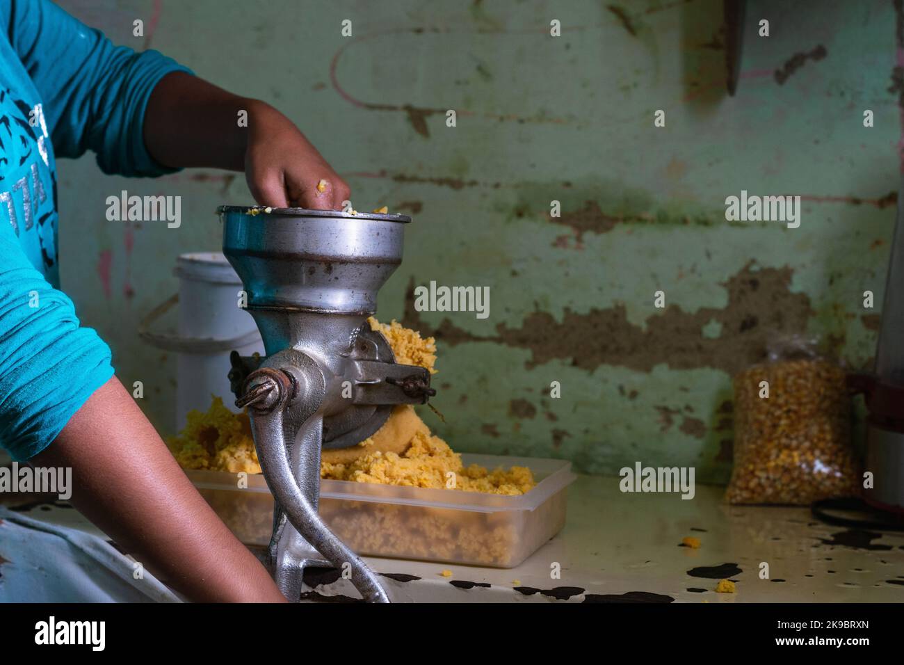 young latina girl with brown skin, grinding cooked corn in a corn ...