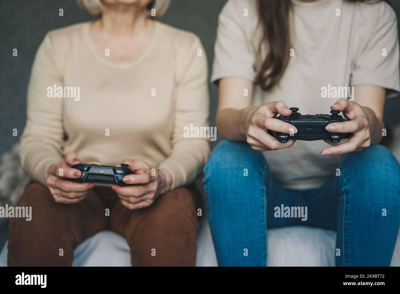 Hands of an old woman and a mature woman holding joysticks playing ...