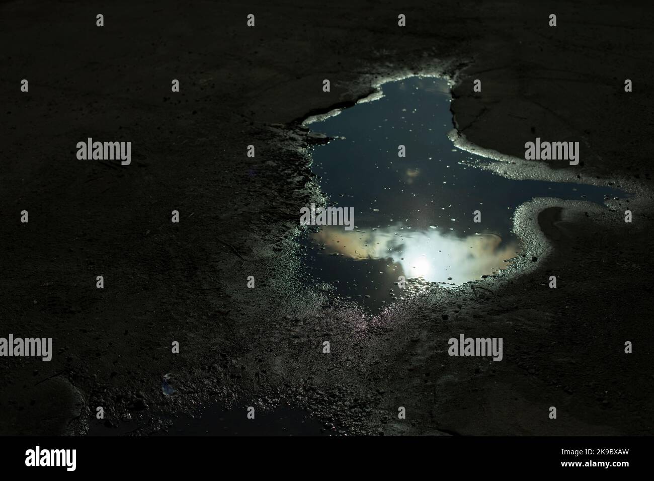 Sun in puddle. Puddle dries on asphalt. Details of road. Water on ...