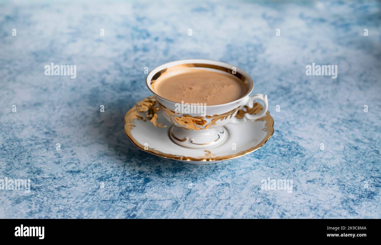 Refined white and gilded coffee cup on an abstract blue background ...
