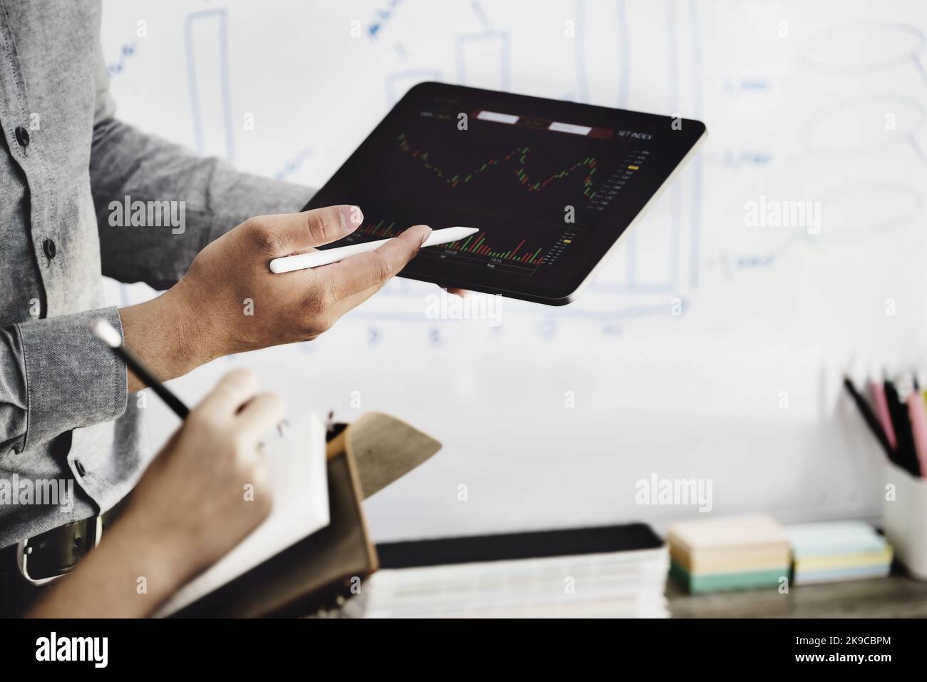 An investment expert points a pen at a tablet monitor to analyze the ...
