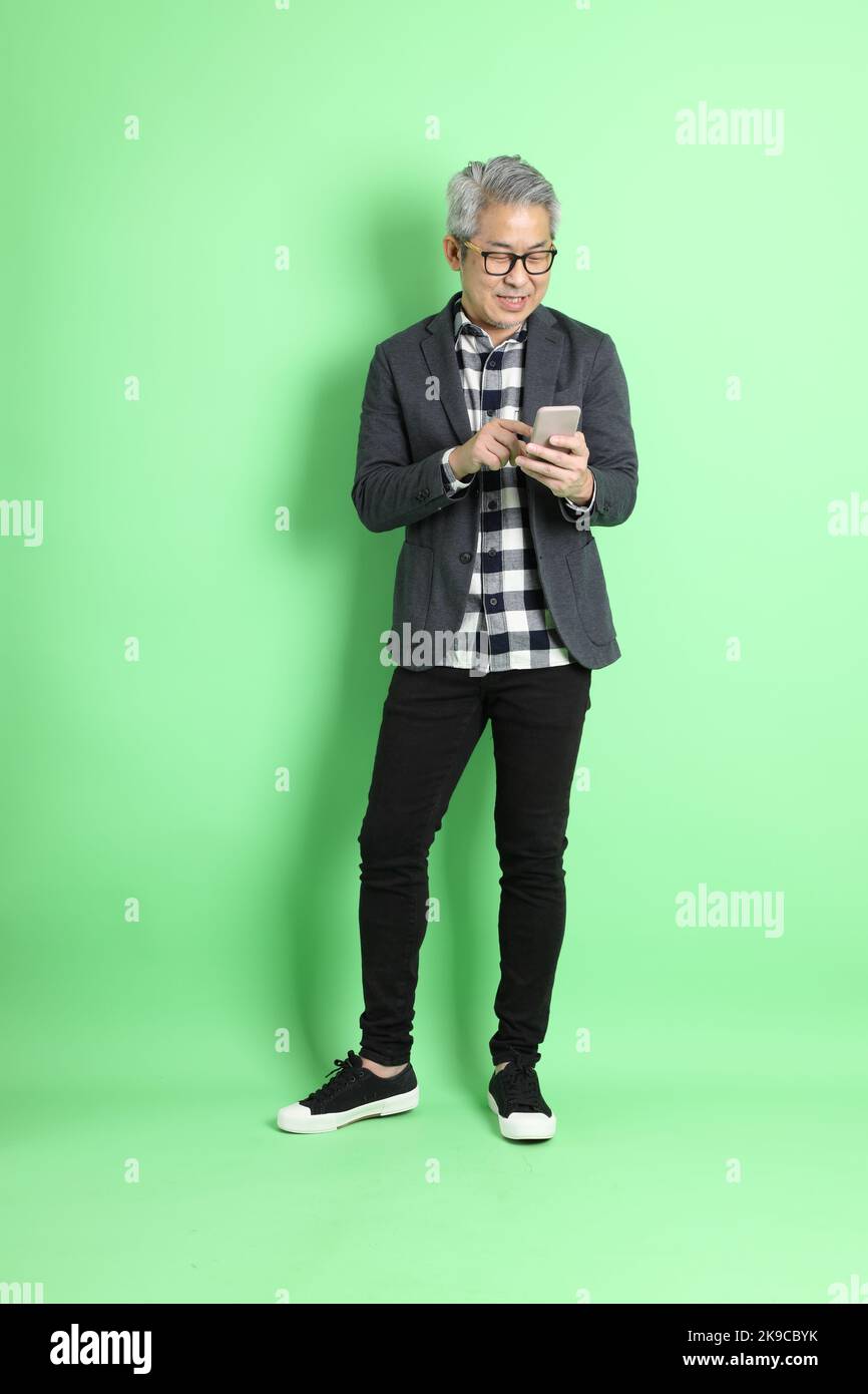 The 40s adult Asian man stnading on the green background with smart ...