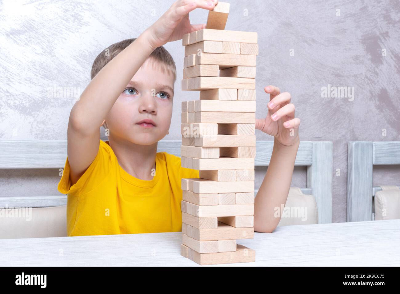 Interested happy little blond boy playing board game taking bricks from ...