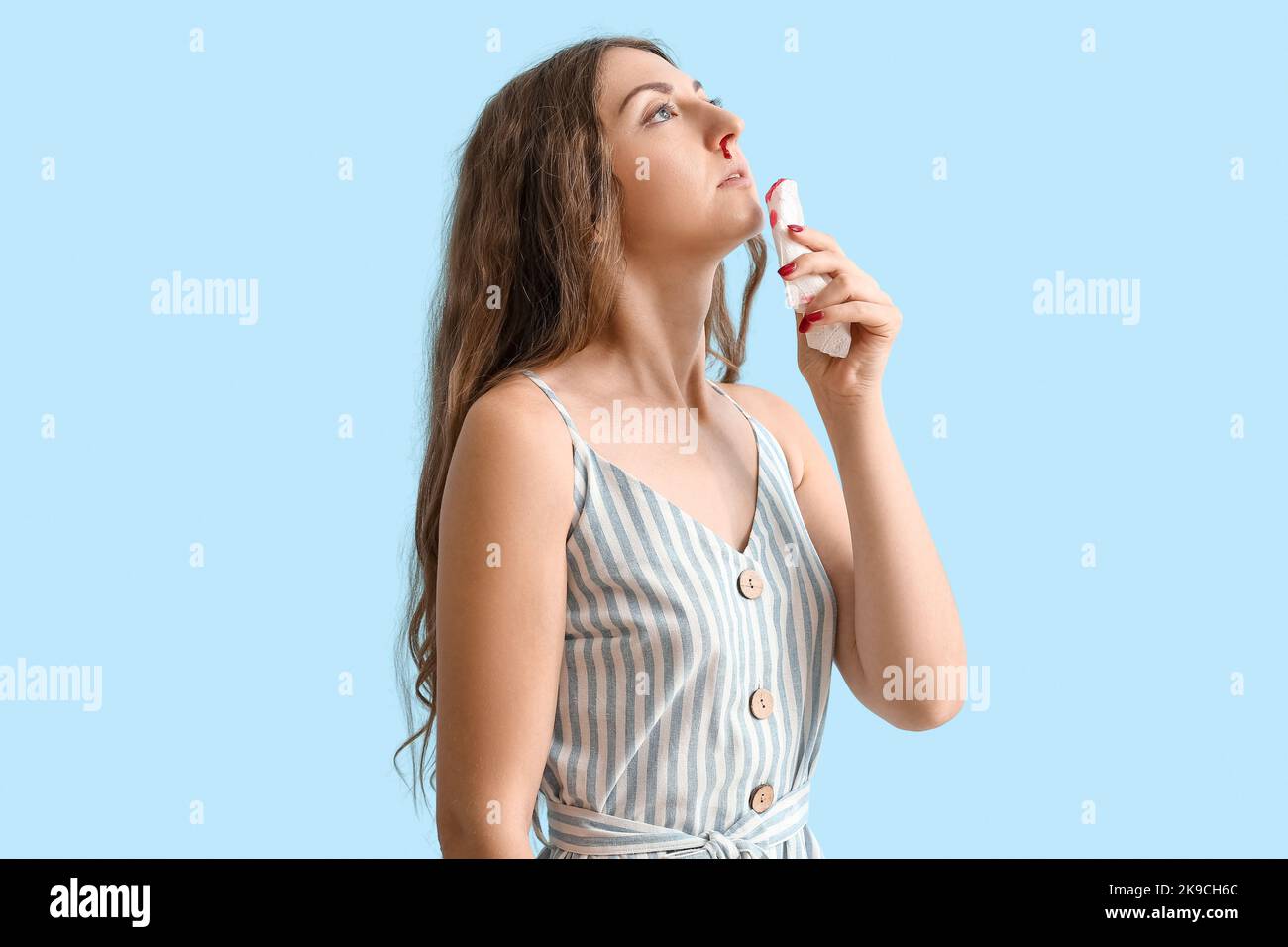 Young woman with nosebleed and tissue on blue background Stock Photo ...