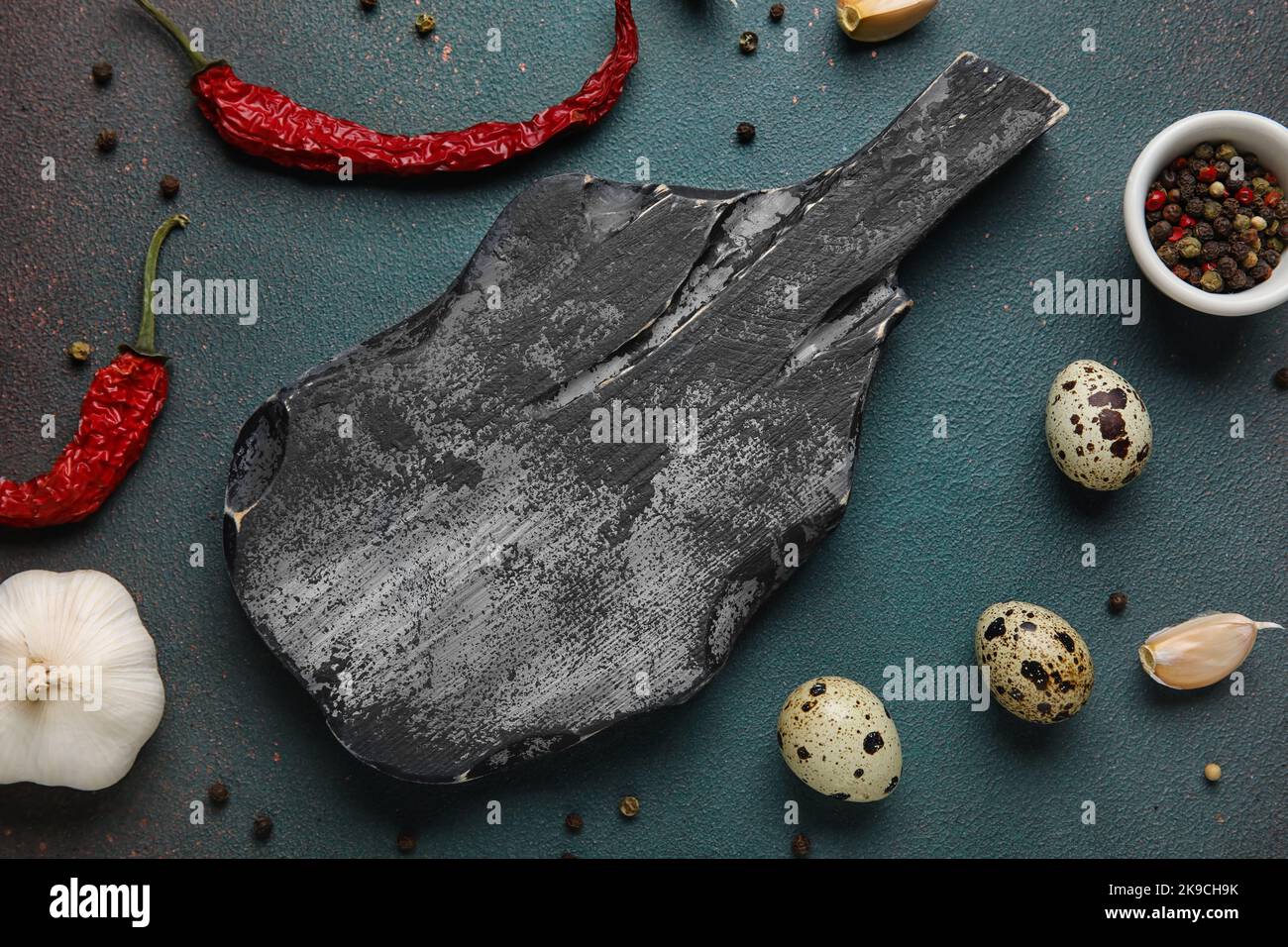 Black wooden cutting board with spices and quail eggs on dark ...