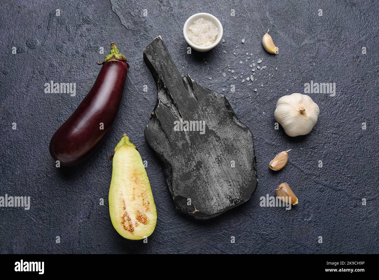 Black wooden cutting board, eggplant and spices on dark background ...