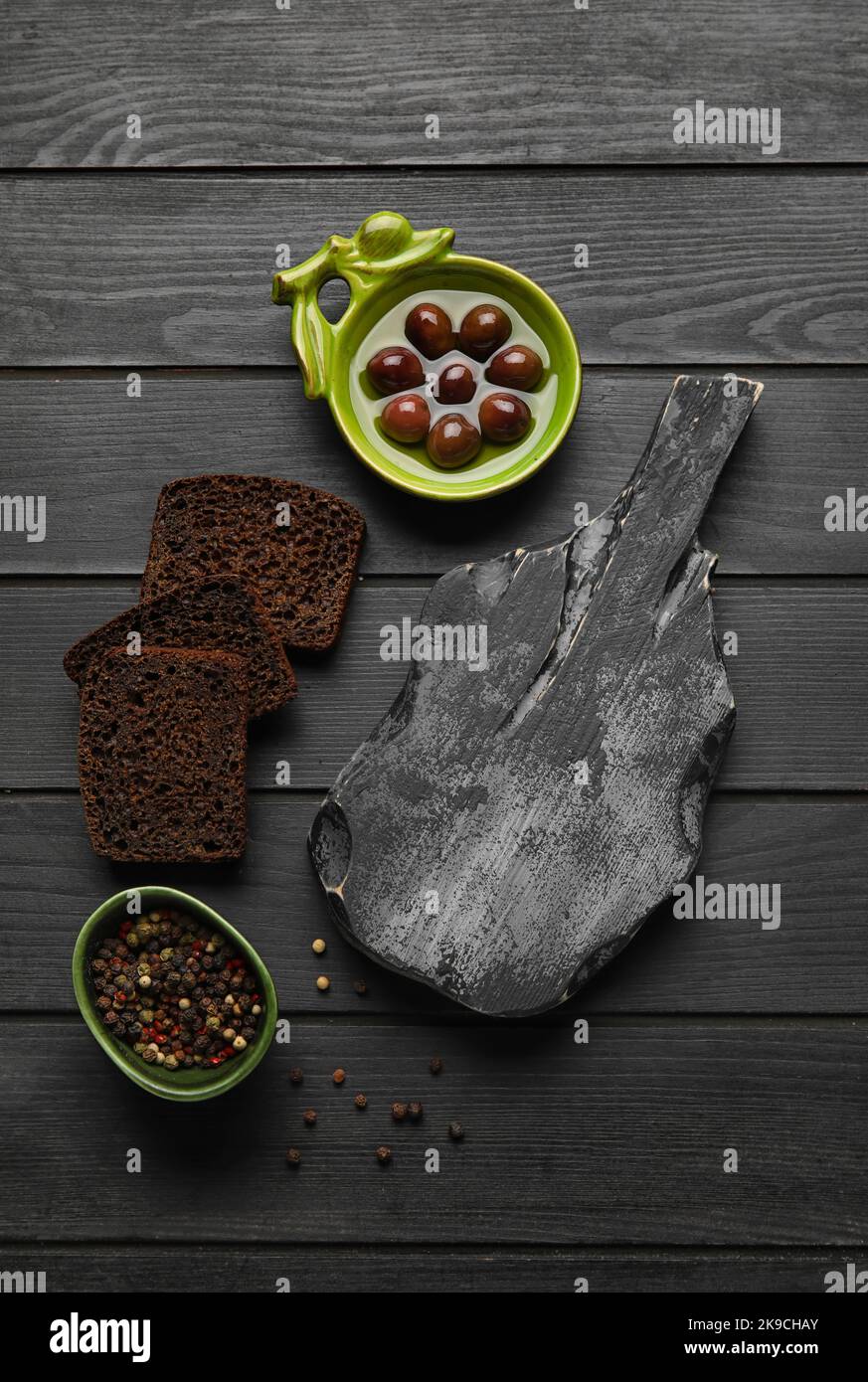 Black cutting board with slices of bread, peppercorns and olives on ...