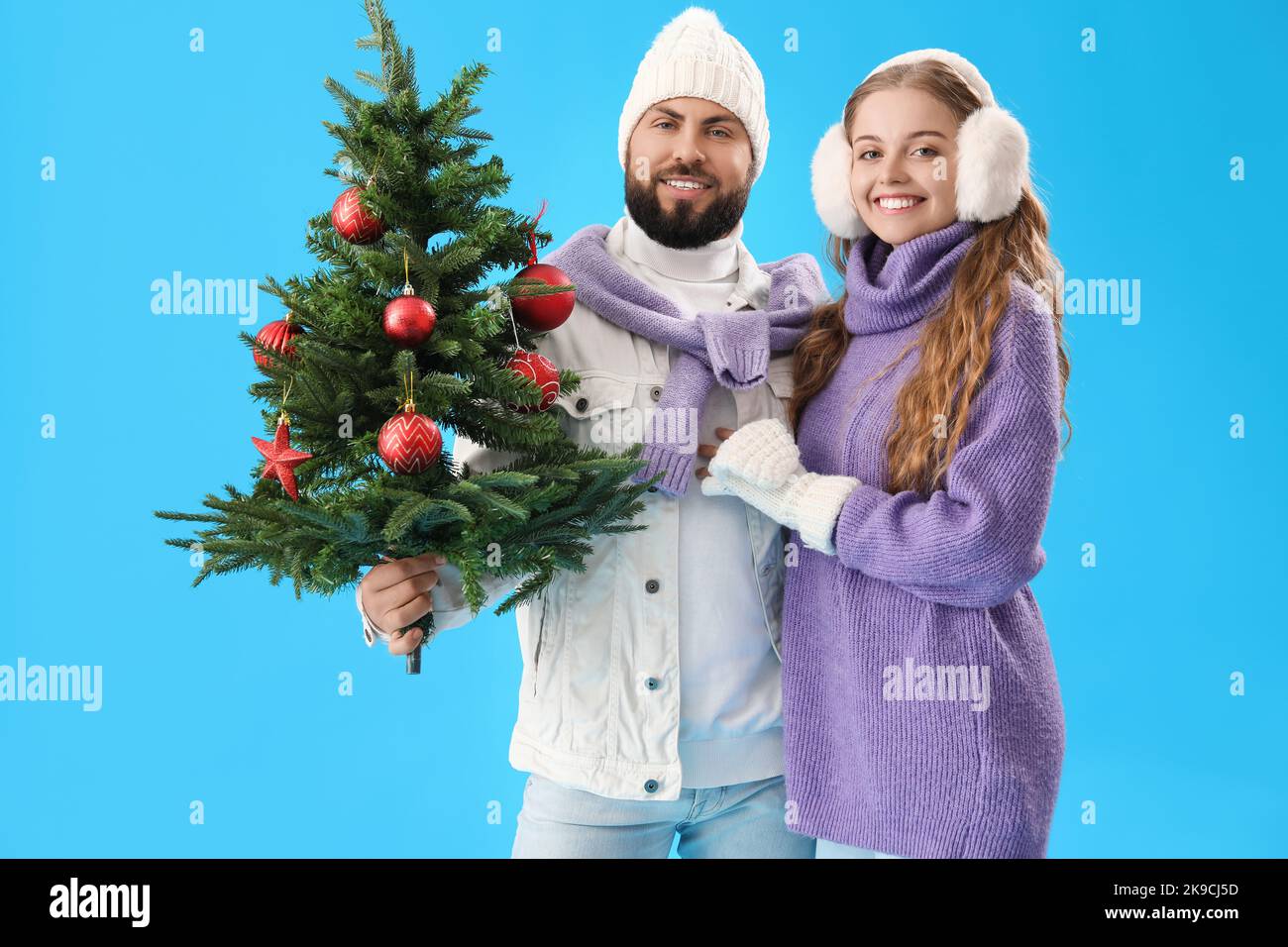 Young couple with Christmas tree on blue background Stock Photo - Alamy