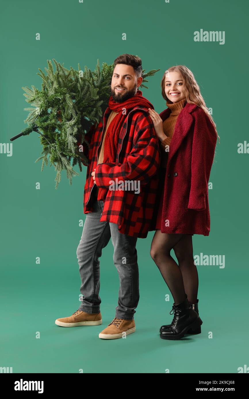 Young couple with Christmas tree on green background Stock Photo - Alamy