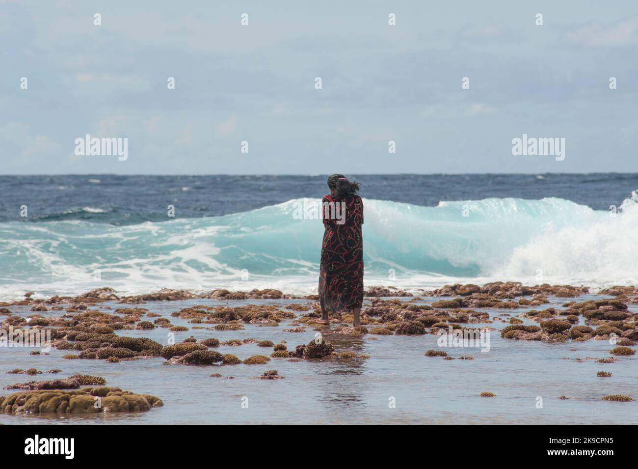 A Marshallese woman walks towards a breaking wave on the ocean-side ...