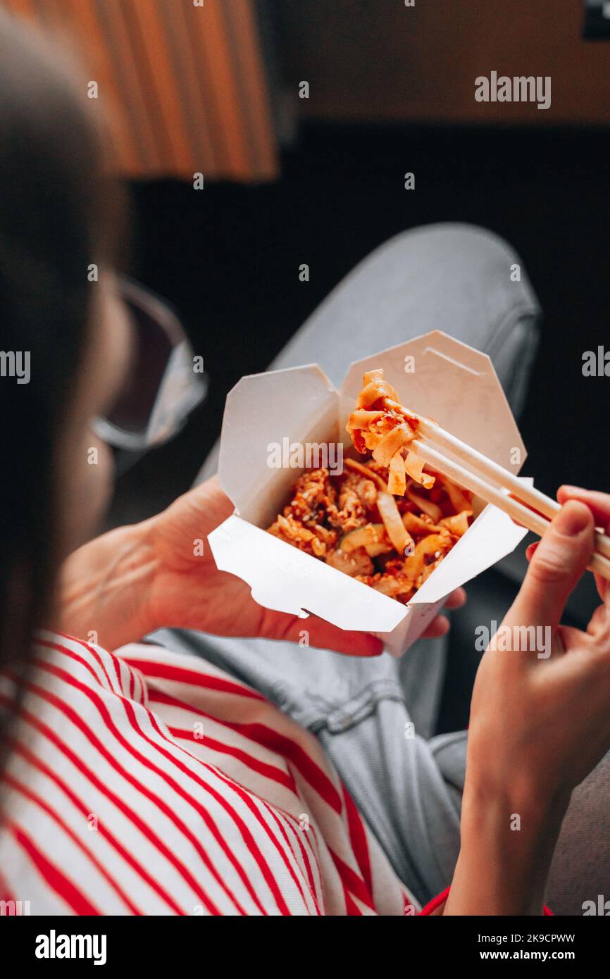 Woman eating fast food from takeaway box asian chinese noodles with ...