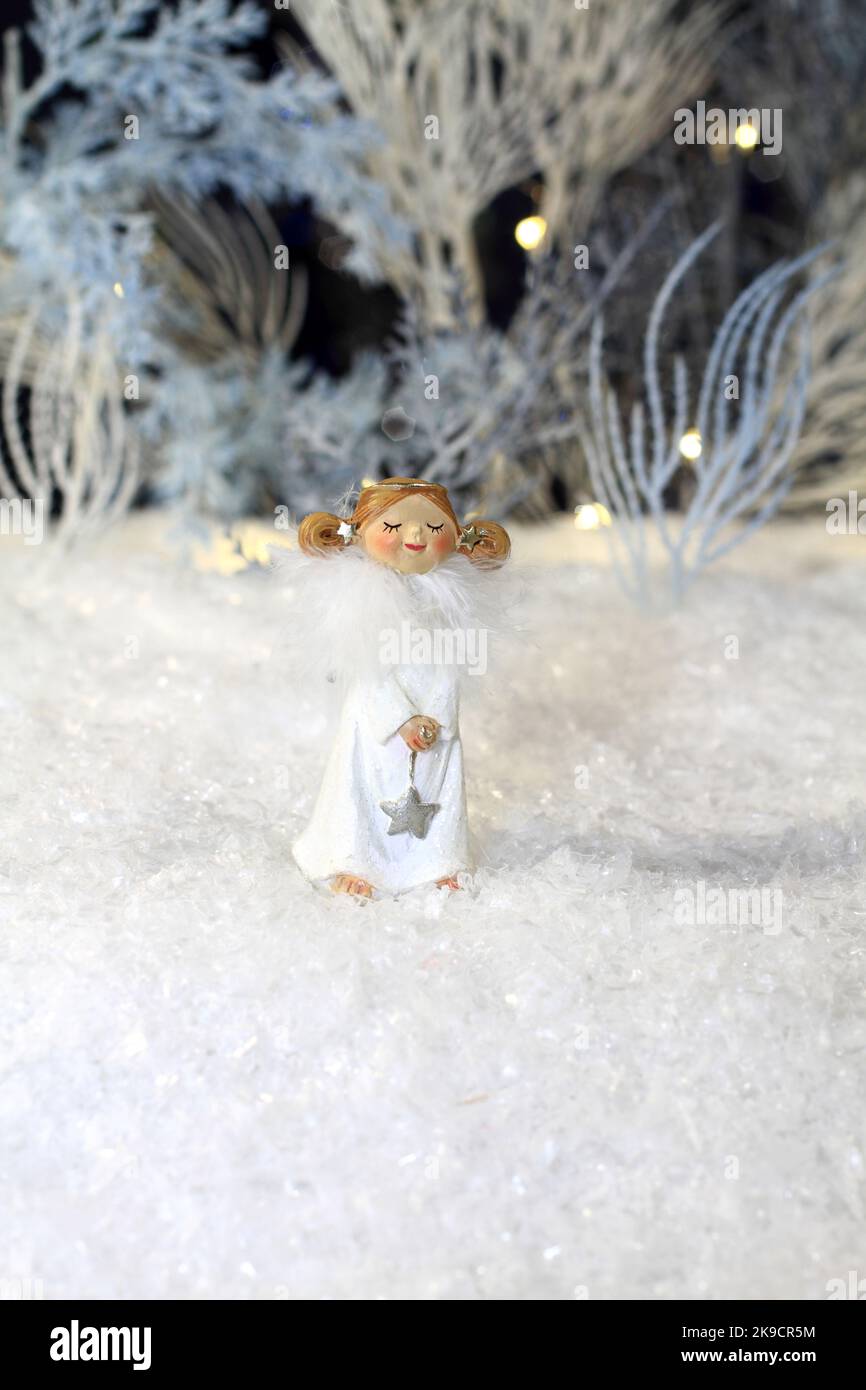 Toy Angel stands on artificial snow and artificial blue and white trees ...