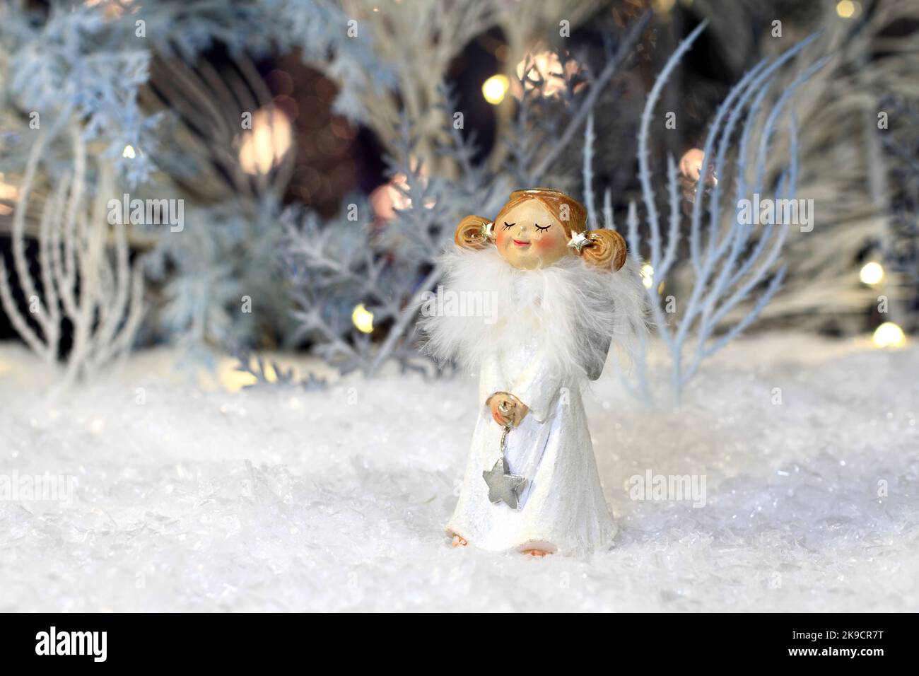 Toy Angel stands on artificial snow and artificial blue and white trees ...