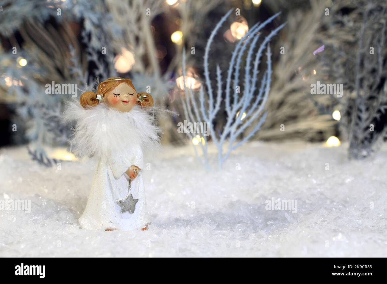 Toy Angel stands on artificial snow and artificial blue and white trees ...