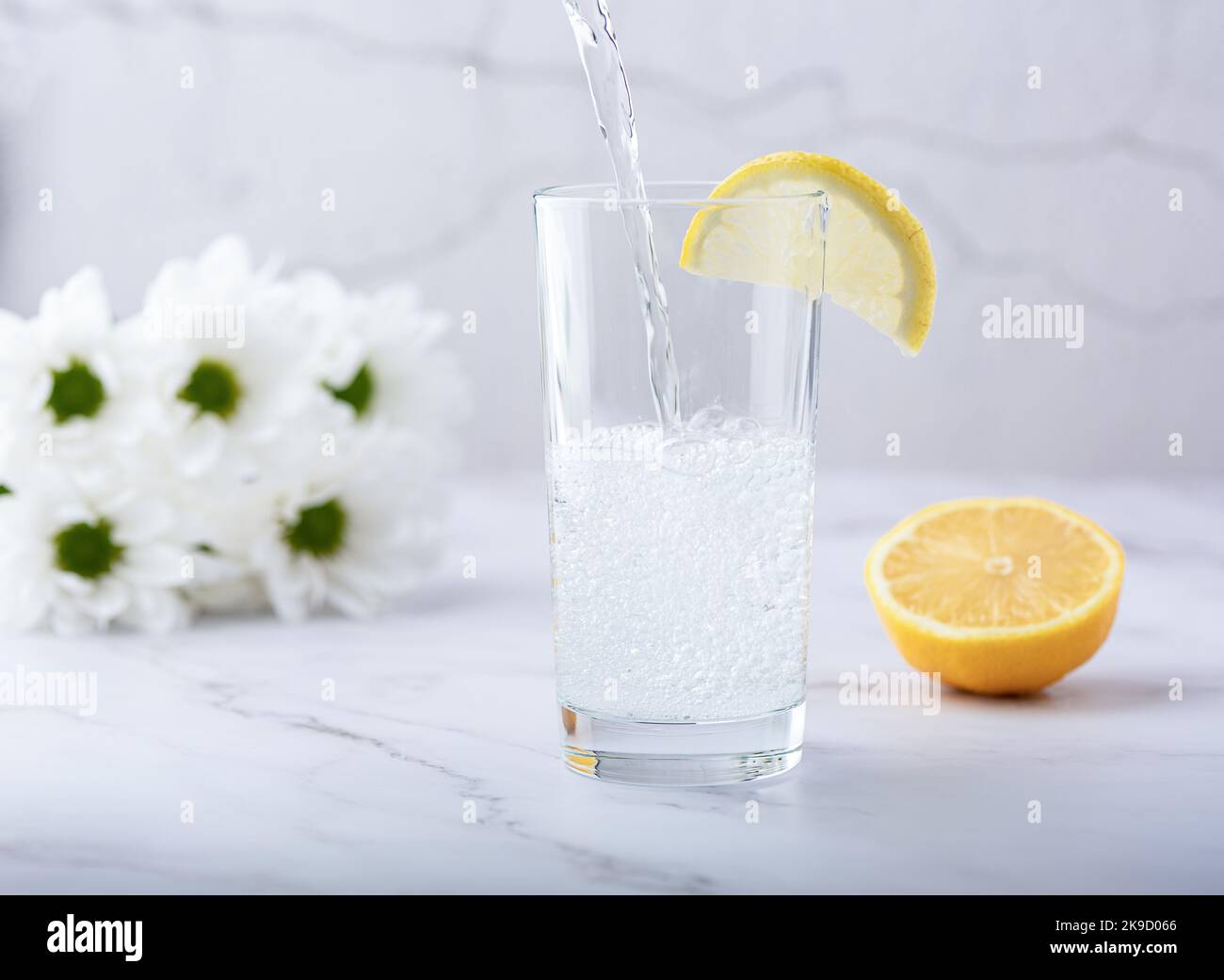 Refreshing mineral water is poured into a glass with a slice of lemon ...
