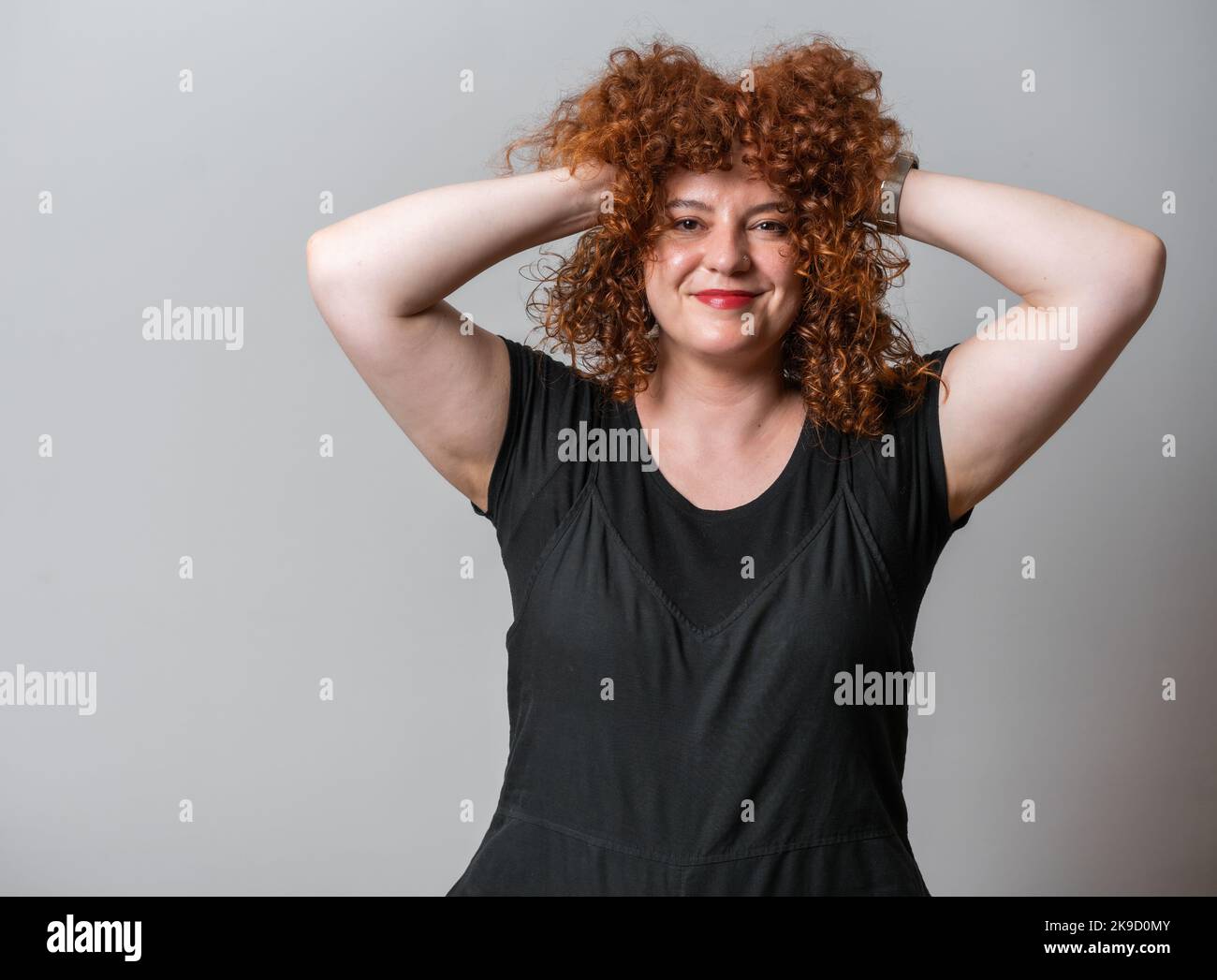 Happy woman with red curly hair posing on grey background, with copy ...