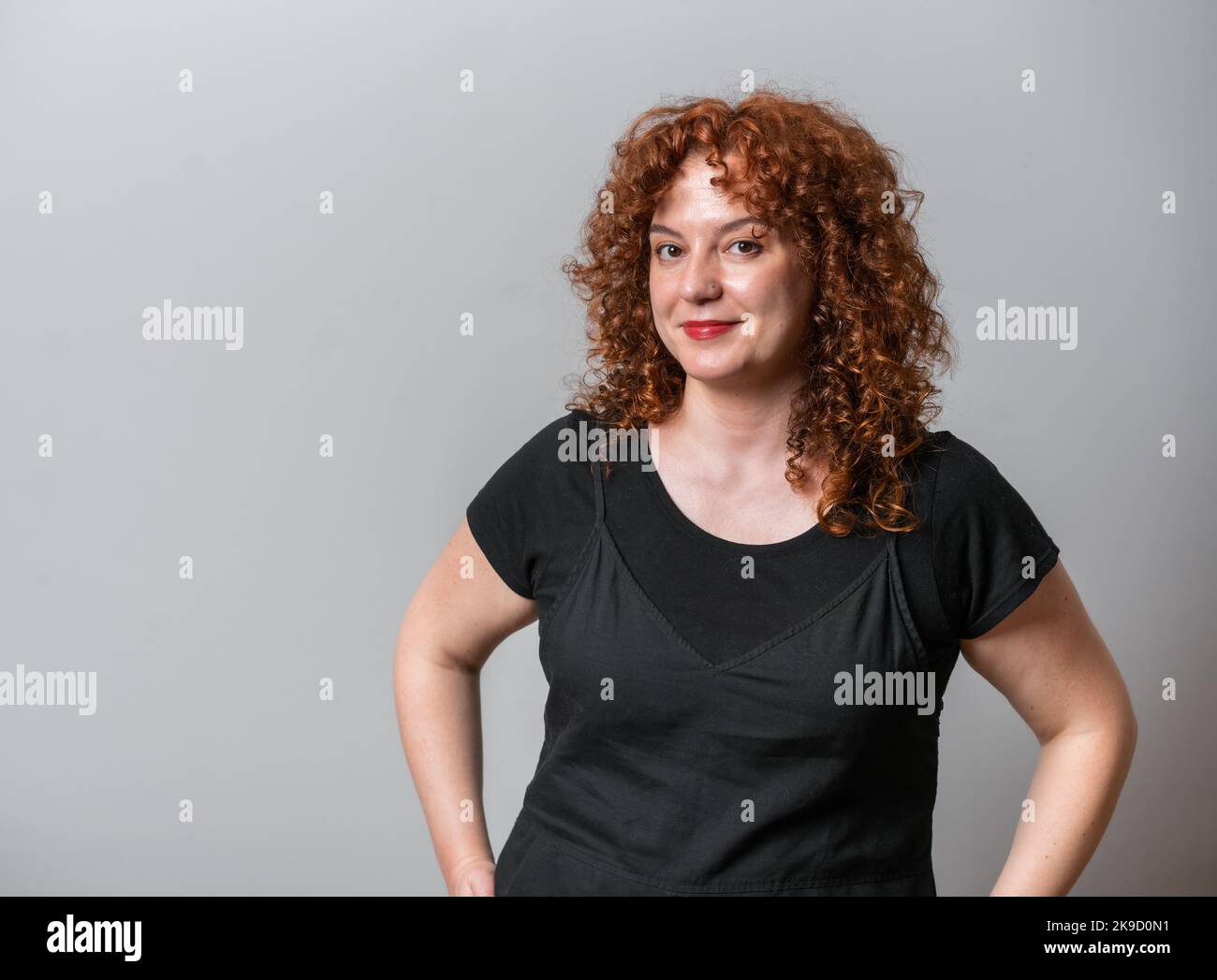 Happy woman with red curly hair posing on grey background, with copy ...