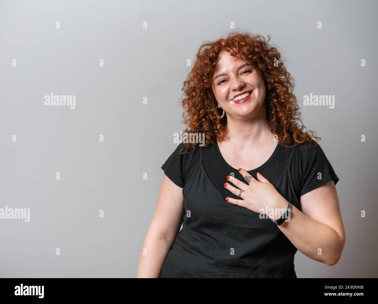 Happy woman with red curly hair posing on grey background, with copy ...