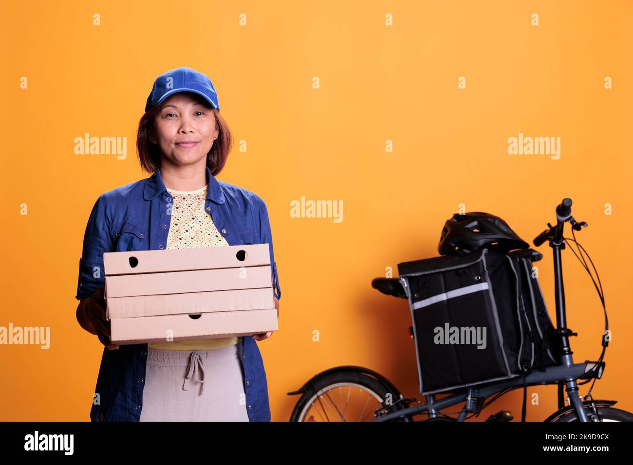 Asian takeout food delivery employee wearing blue uniform holding stack ...