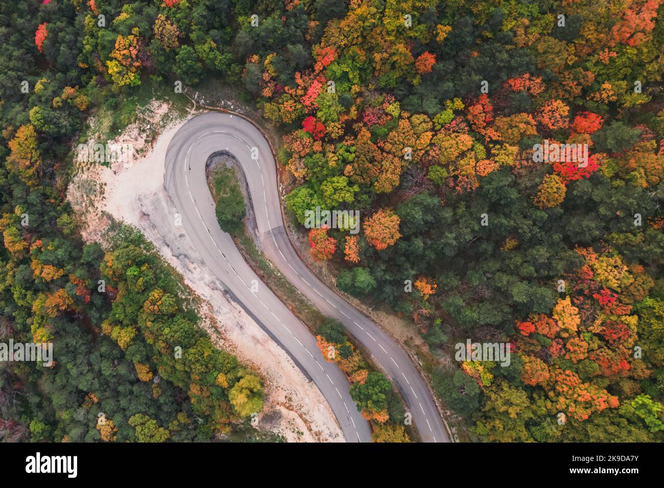 Aerial view of a winding road from a high mountain pass through a dense colorful autumn forest ...