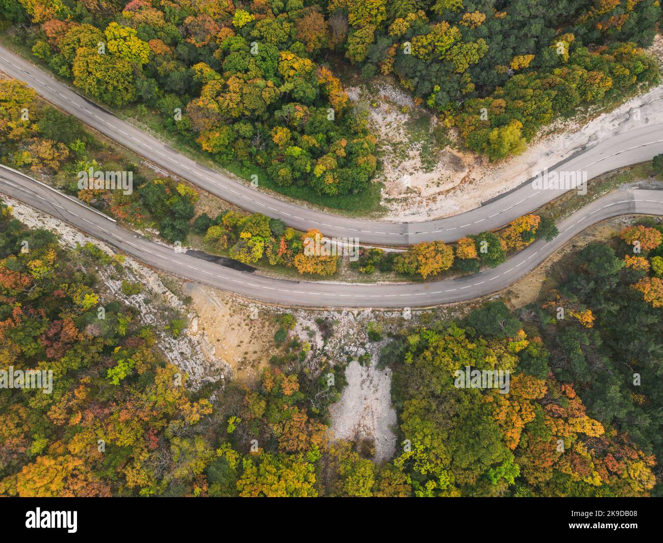 Aerial view of a winding road from a high mountain pass through a dense colorful autumn forest ...