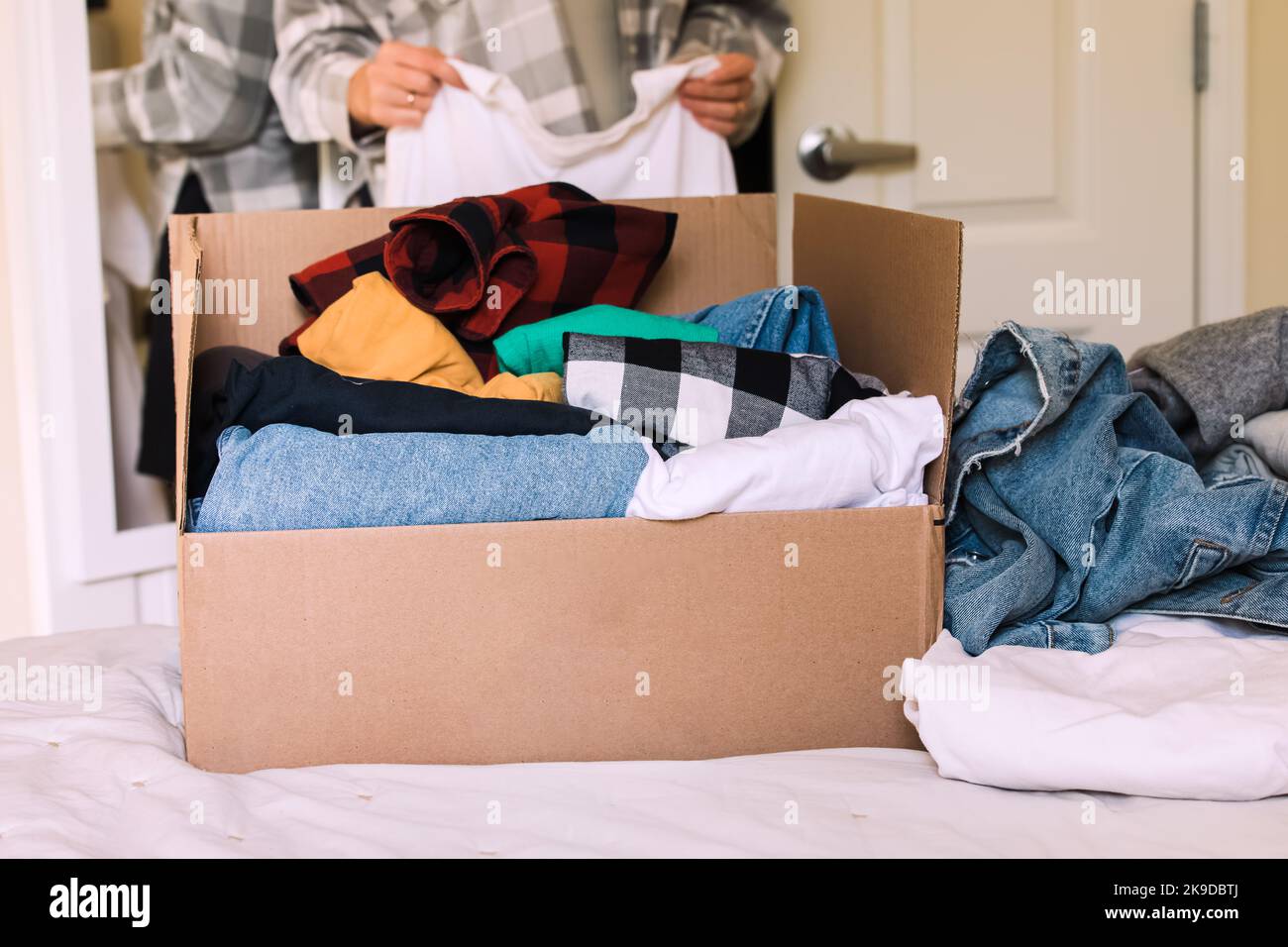 Cardboard box full of clothes and woman on the background. Sorting ...
