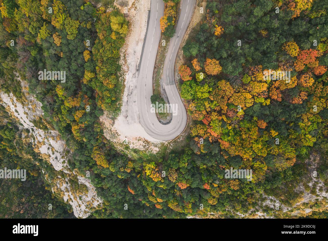 Aerial view of a winding road from a high mountain pass through a dense colorful autumn forest ...