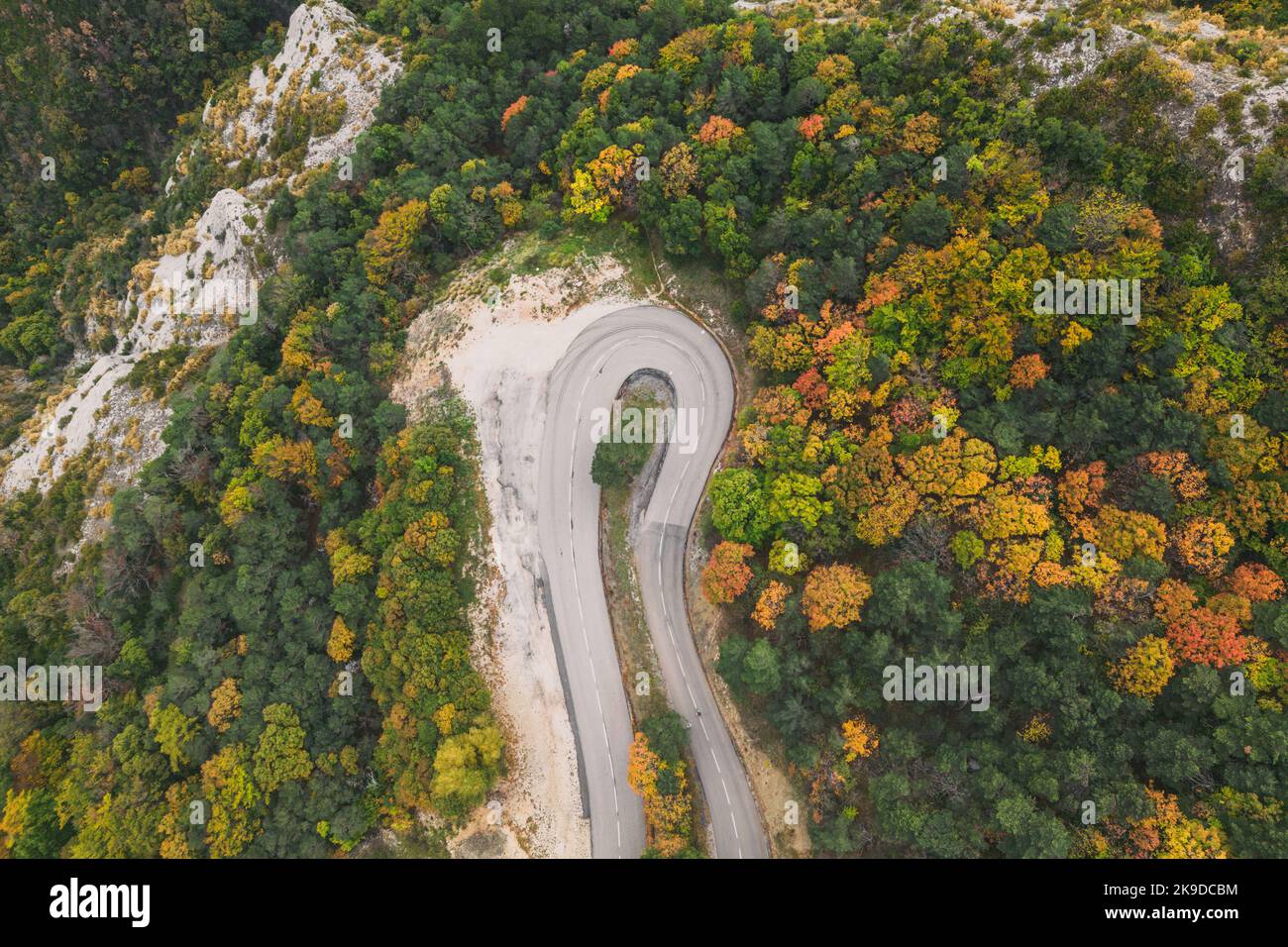 Aerial view of a winding road from a high mountain pass through a dense colorful autumn forest ...