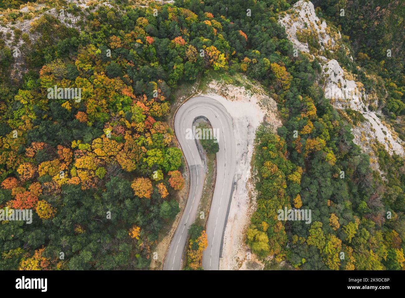 Aerial view of a winding road from a high mountain pass through a dense colorful autumn forest ...