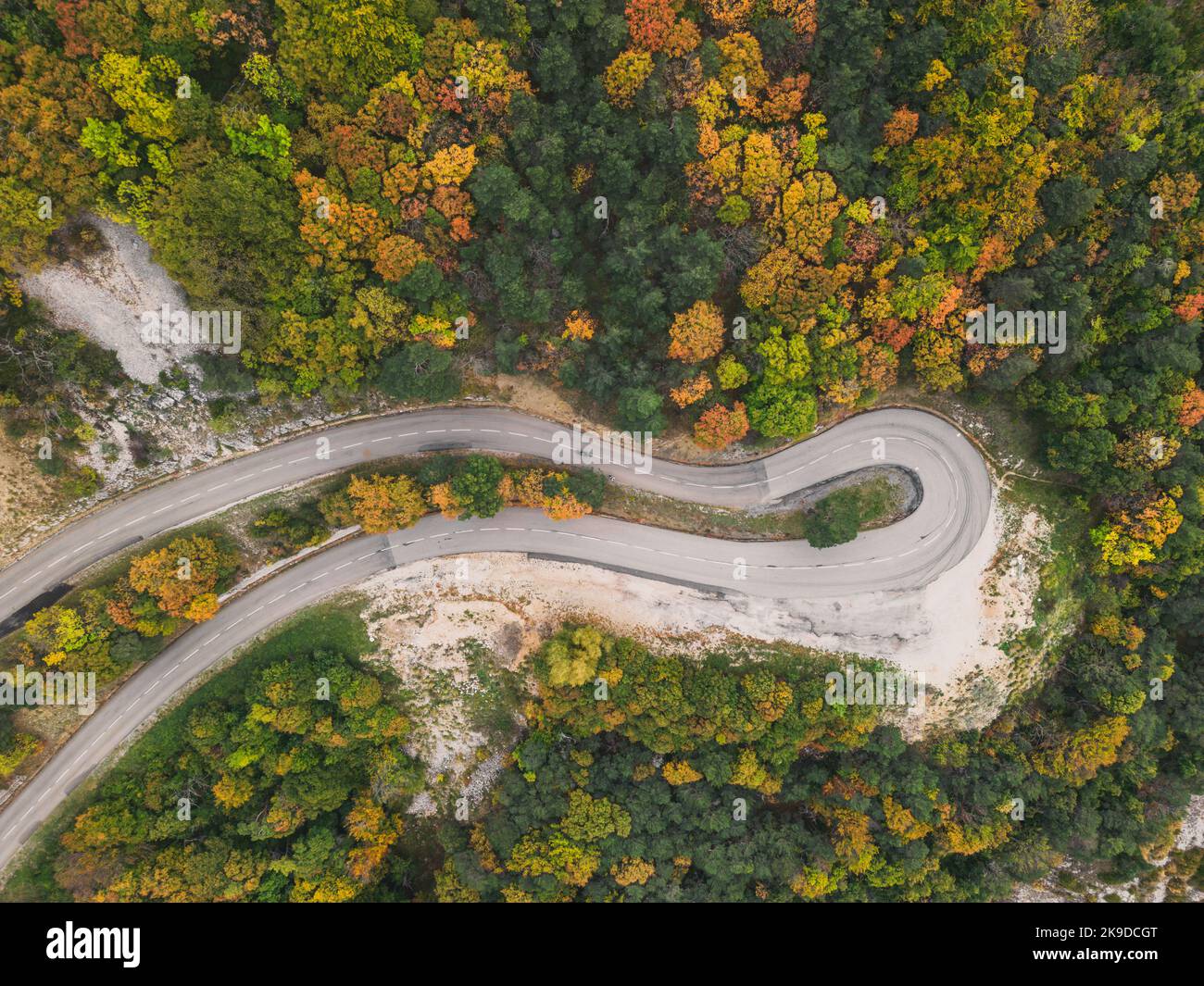 Aerial view of a winding road from a high mountain pass through a dense colorful autumn forest ...
