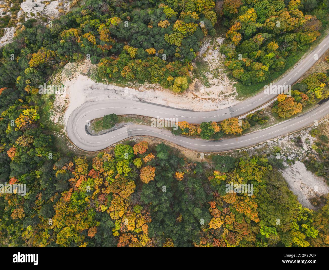 Aerial view of a winding road from a high mountain pass through a dense colorful autumn forest ...