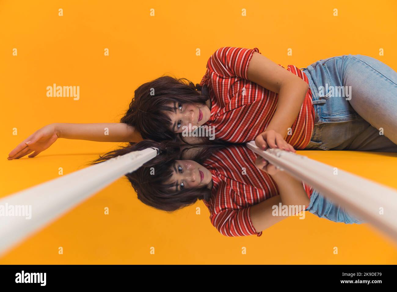 White young woman with long dark hair lying on the ground smiling looking at camera reflecting ...