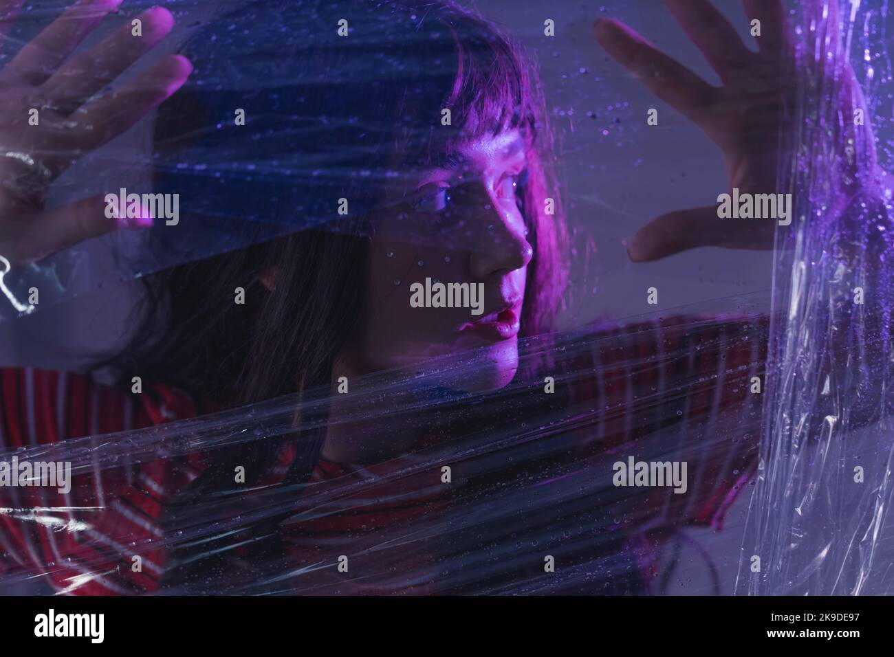 Caucasian young adult woman trapped behind layer of plastic wrap ...