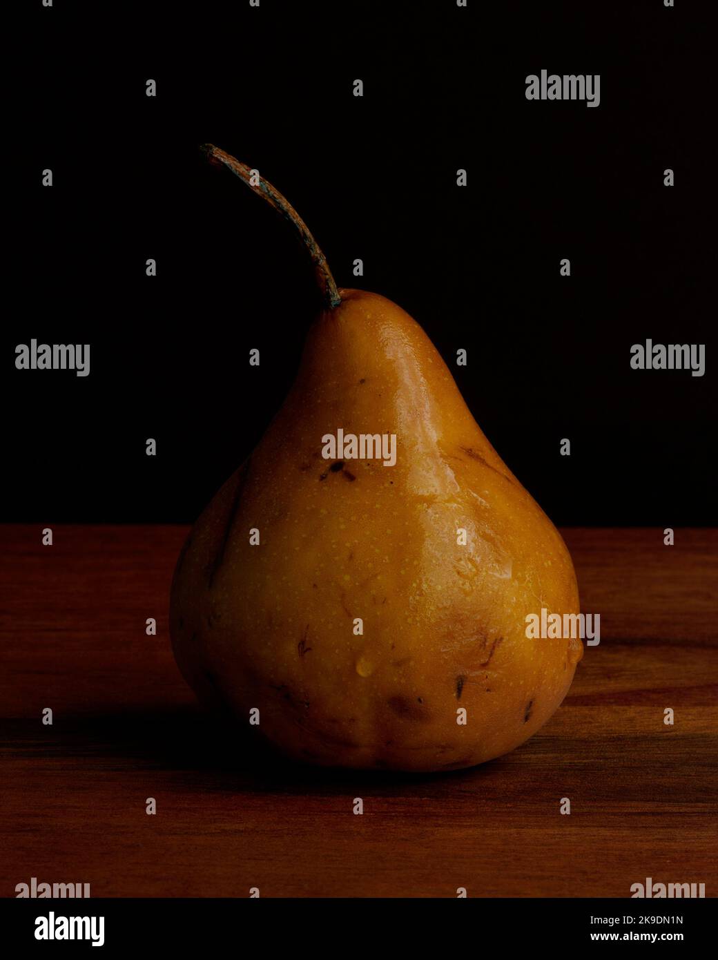 A ripe brown bosc pear on a mahogany table with a black background ...