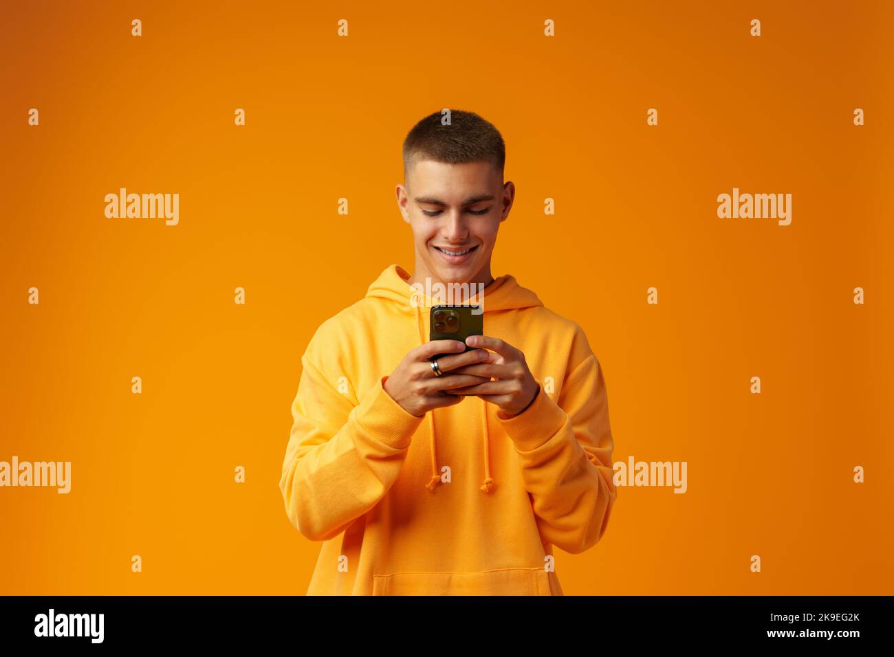 Portrait of a smiling young man holding mobile phone on yellow ...